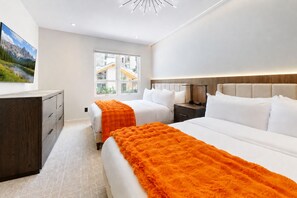 Quarto de hotel com duas camas, uma cômoda, uma mesa de cabeceira e uma janela grande com vista para prédios.
