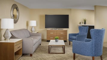 Uma sala de estar moderna com um sofá, duas poltronas, uma mesa de centro, uma TV de tela plana, uma mesinha de cabeceira com uma luminária e um espelho decorativo.