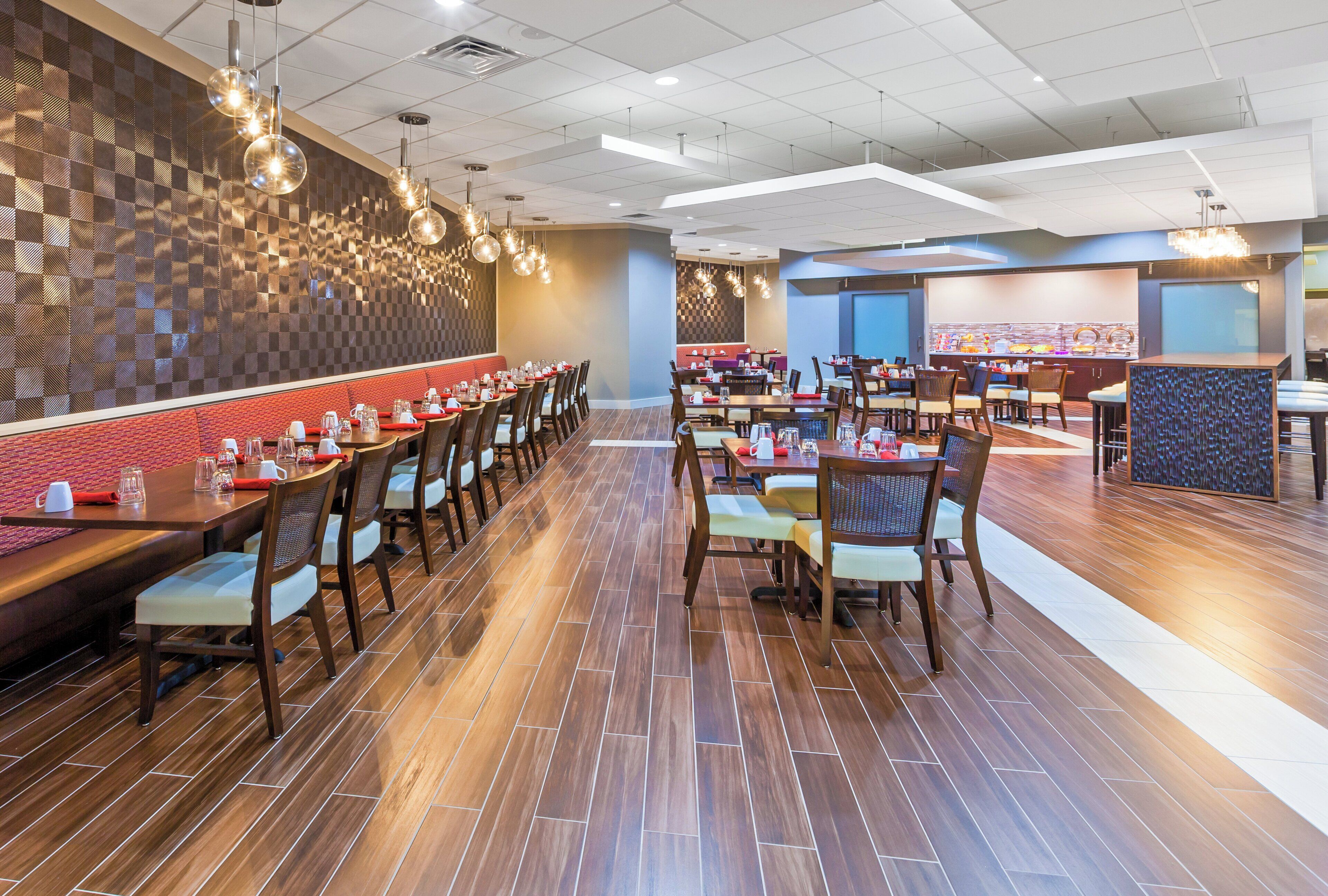 Um restaurante com várias mesas e cadeiras, parede estampada e luminárias pendentes.