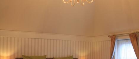 Quarto com cama, duas luminárias de cabeceira, um candelabro, janela com cortinas e radiador.