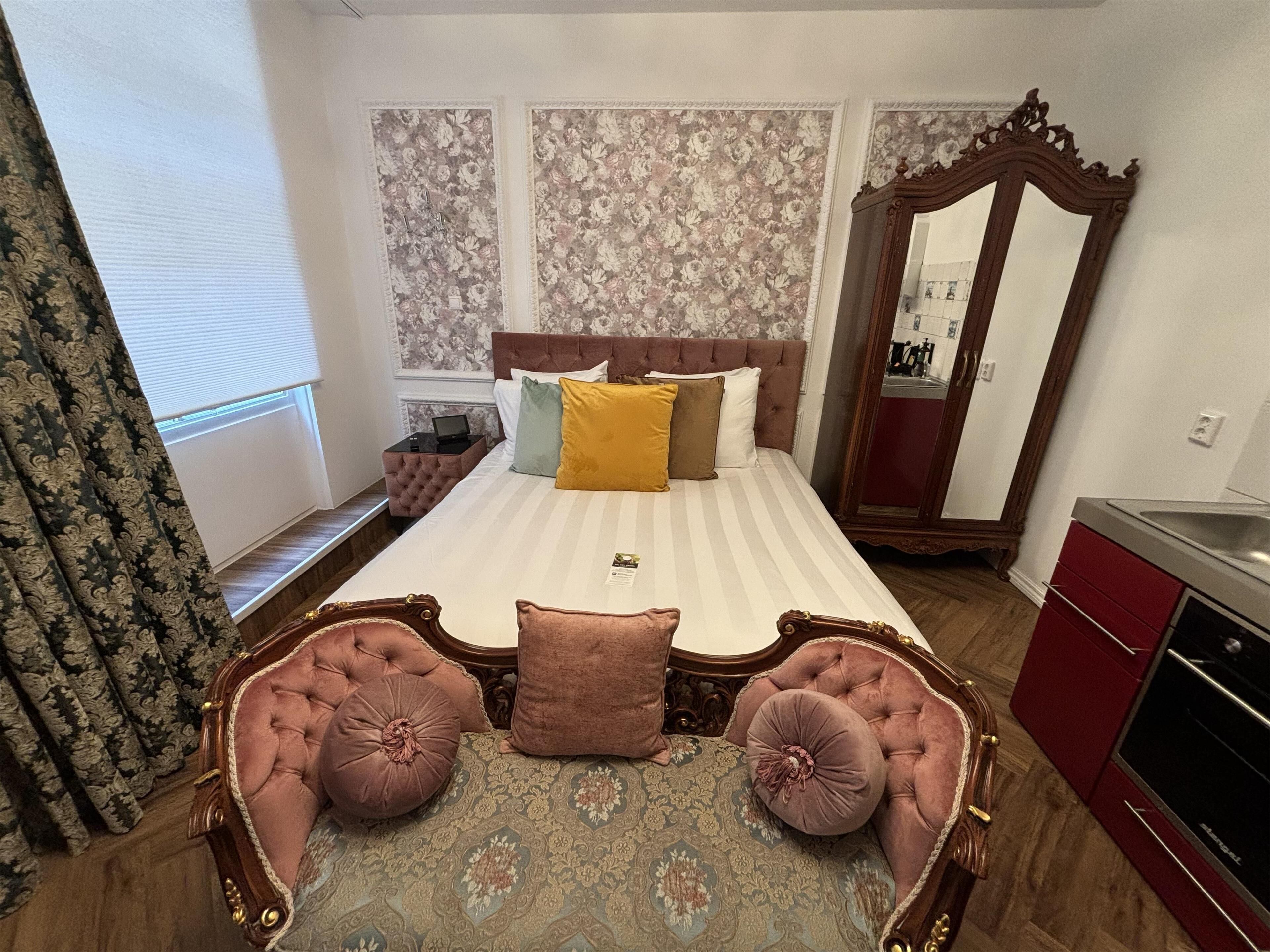 Quarto com uma cama grande, cabeceira de madeira, espelho, cômoda e tapete estampado.