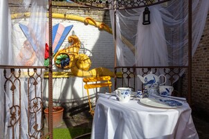 Pátio com uma mesa posta para chá, cercado por uma grade de ferro forjado e uma parede de tijolos.
