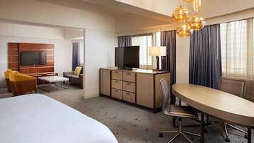 Quarto de hotel com cama, escrivaninha com televisão, cadeira, mesa de jantar e luminária.