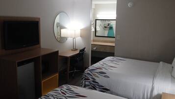 Quarto de hotel com duas camas, uma mesa com abajur, televisão e banheiro visível por uma porta aberta.