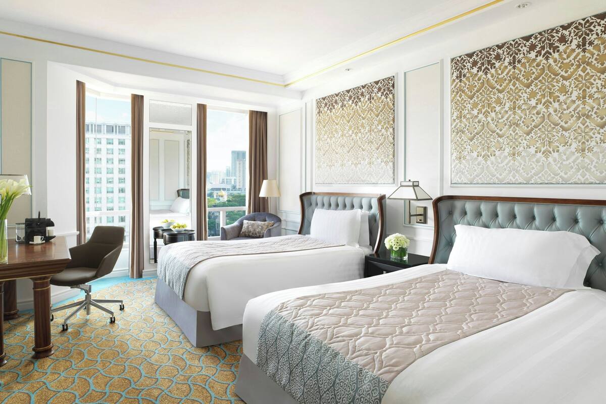 Quarto de hotel com duas camas, uma escrivaninha, uma cadeira, um criado-mudo e vista para a cidade.