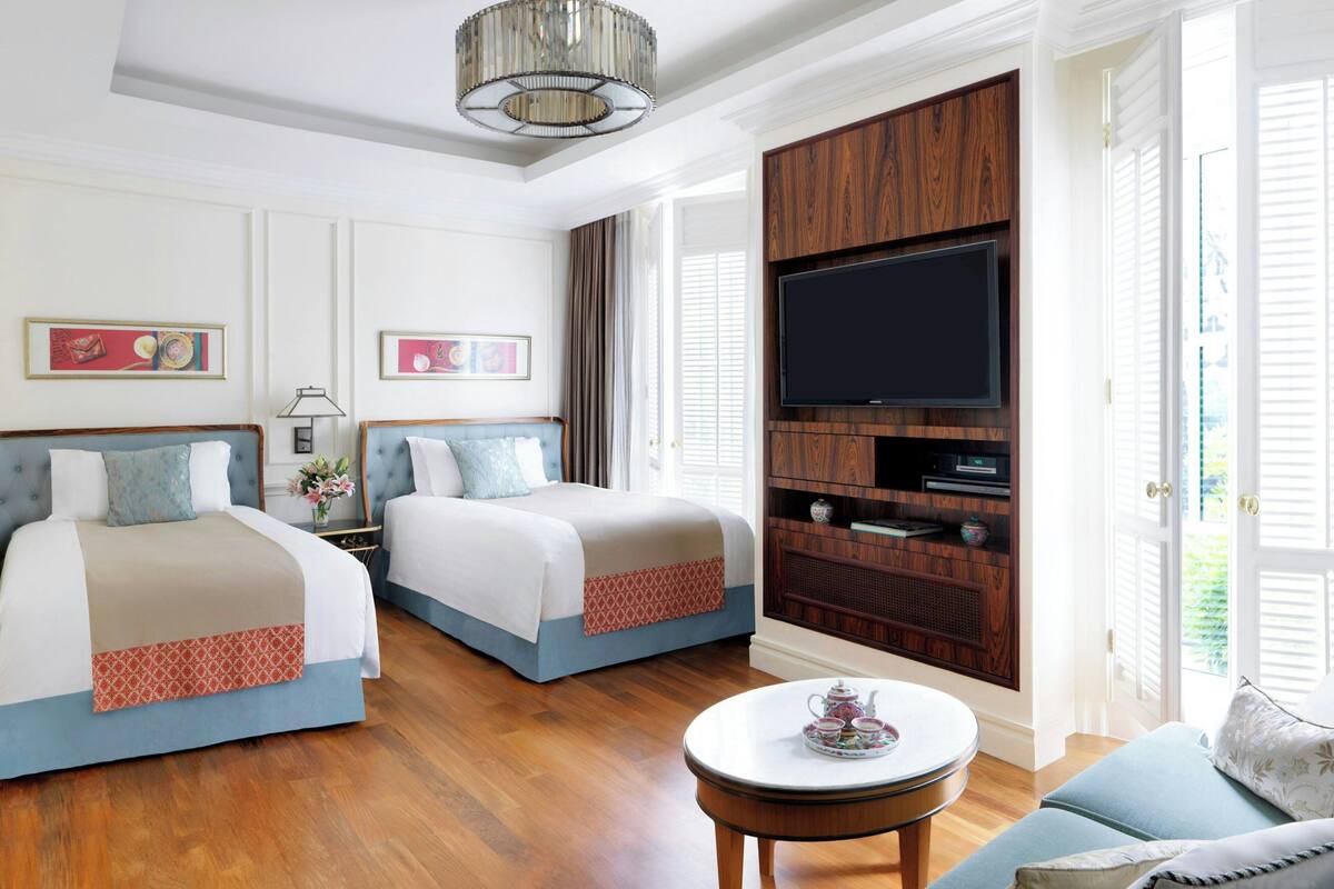 Quarto de hotel com duas camas, uma televisão, uma pequena mesa e um sofá.