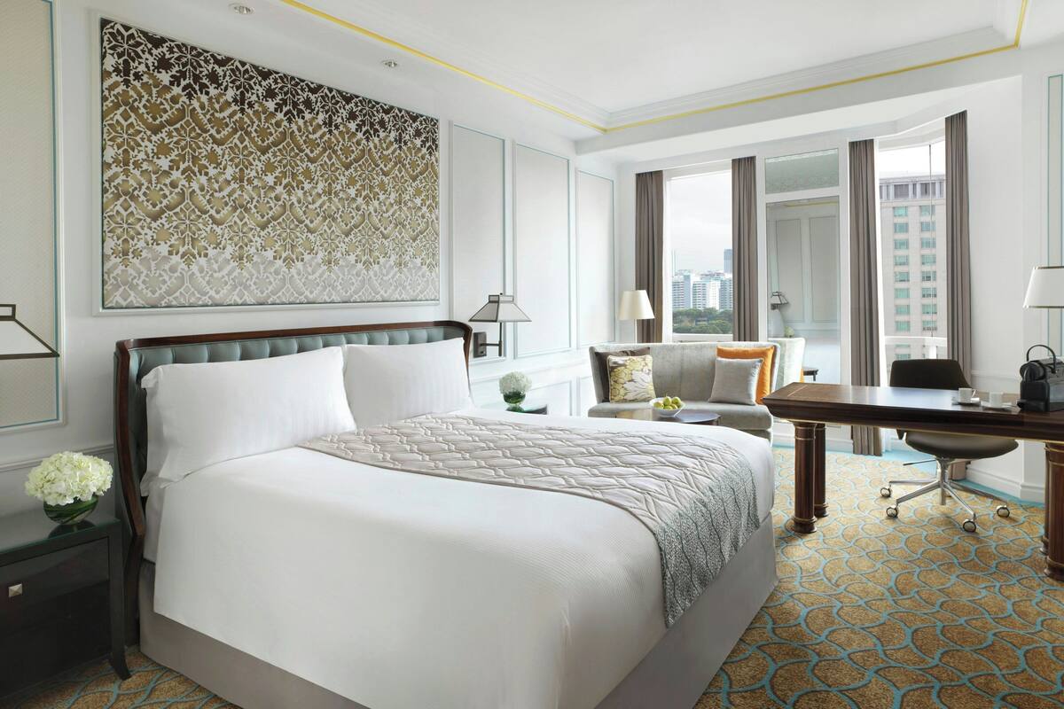 Quarto de hotel com cama grande, escrivaninha, cadeira e vista da cidade.