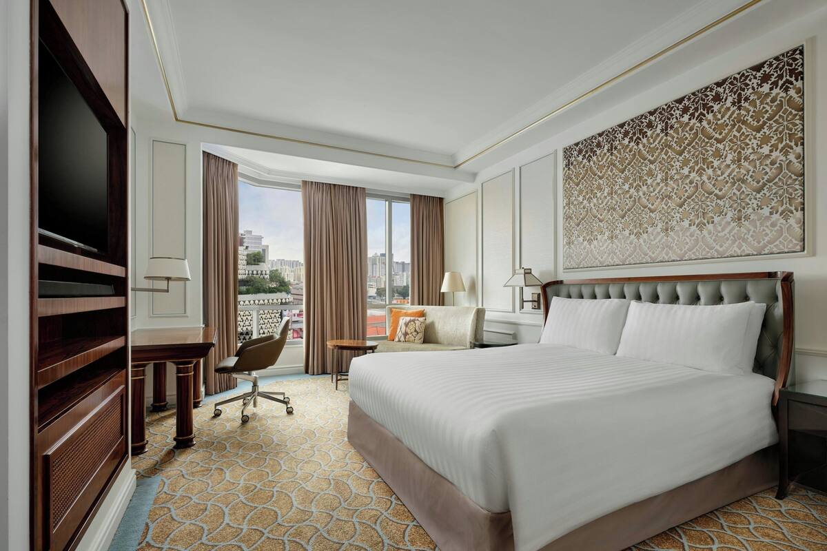 Quarto de hotel com uma cama grande, uma escrivaninha, uma cadeira, televisão e vista para a cidade.