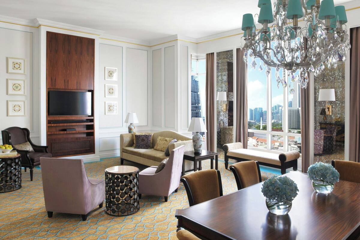 Quarto de hotel moderno com uma grande mesa de jantar, assentos confortáveis, televisão e vista para a cidade.