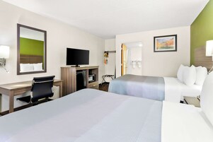 Quarto de hotel com duas camas, uma escrivaninha com cadeira, televisão, espelho e um quadro na parede.