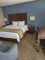 Quarto de hotel com uma cama grande, mesas de cabeceira, uma escrivaninha e uma cadeira.