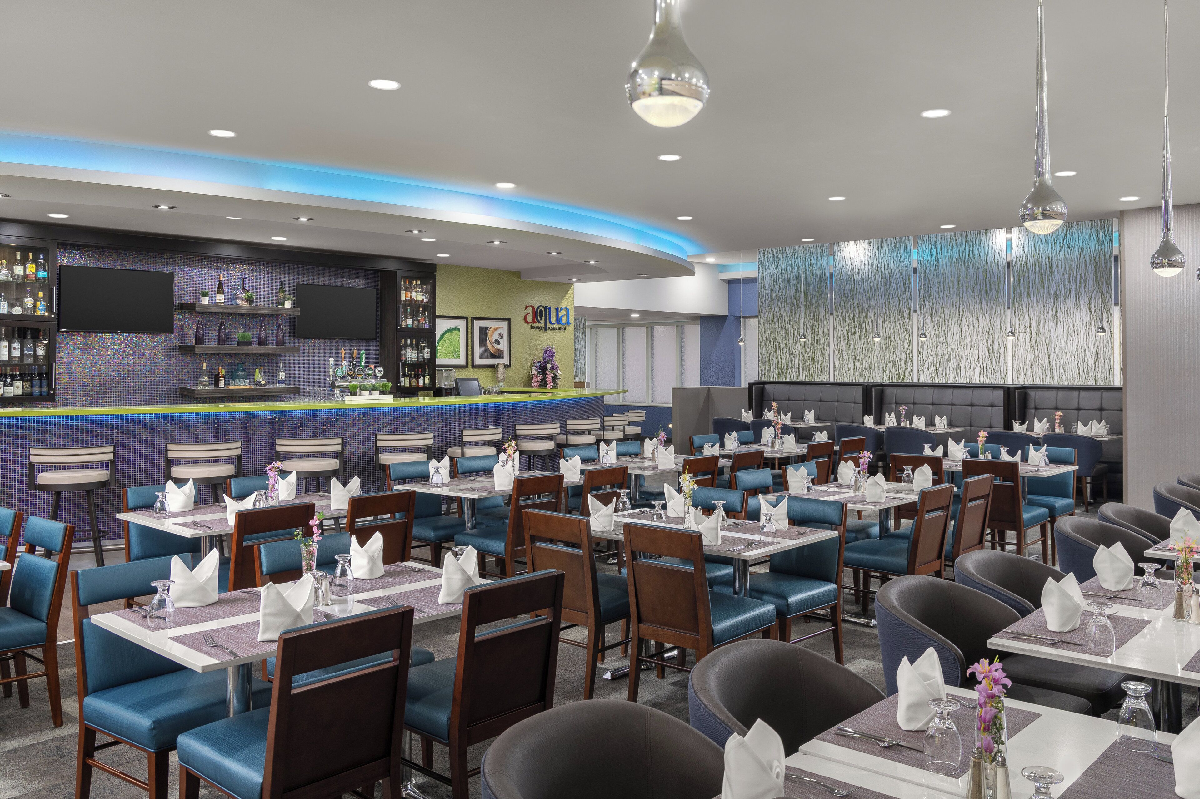 Um restaurante com várias mesas, cadeiras, um bar e uma parede decorativa.