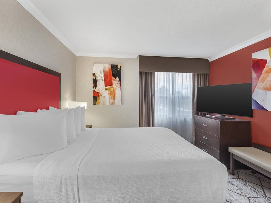 Quarto de hotel com cama grande, televisão, um banquinho e um quadro na parede.