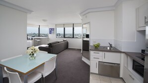 Apartamento moderno com área de jantar, sofá, cozinha e grandes janelas com vista para a cidade.