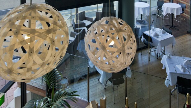 Um interior moderno com grandes janelas, móveis de madeira e luminárias pendentes.