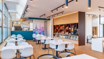 Um restaurante moderno com um balcão extenso, cadeiras brancas e um mural com a silhueta de um horizonte urbano.