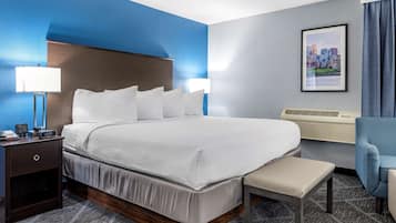 Quarto de hotel com uma cama grande, mesas de cabeceira, uma cadeira e uma pintura de paisagem urbana na parede.
