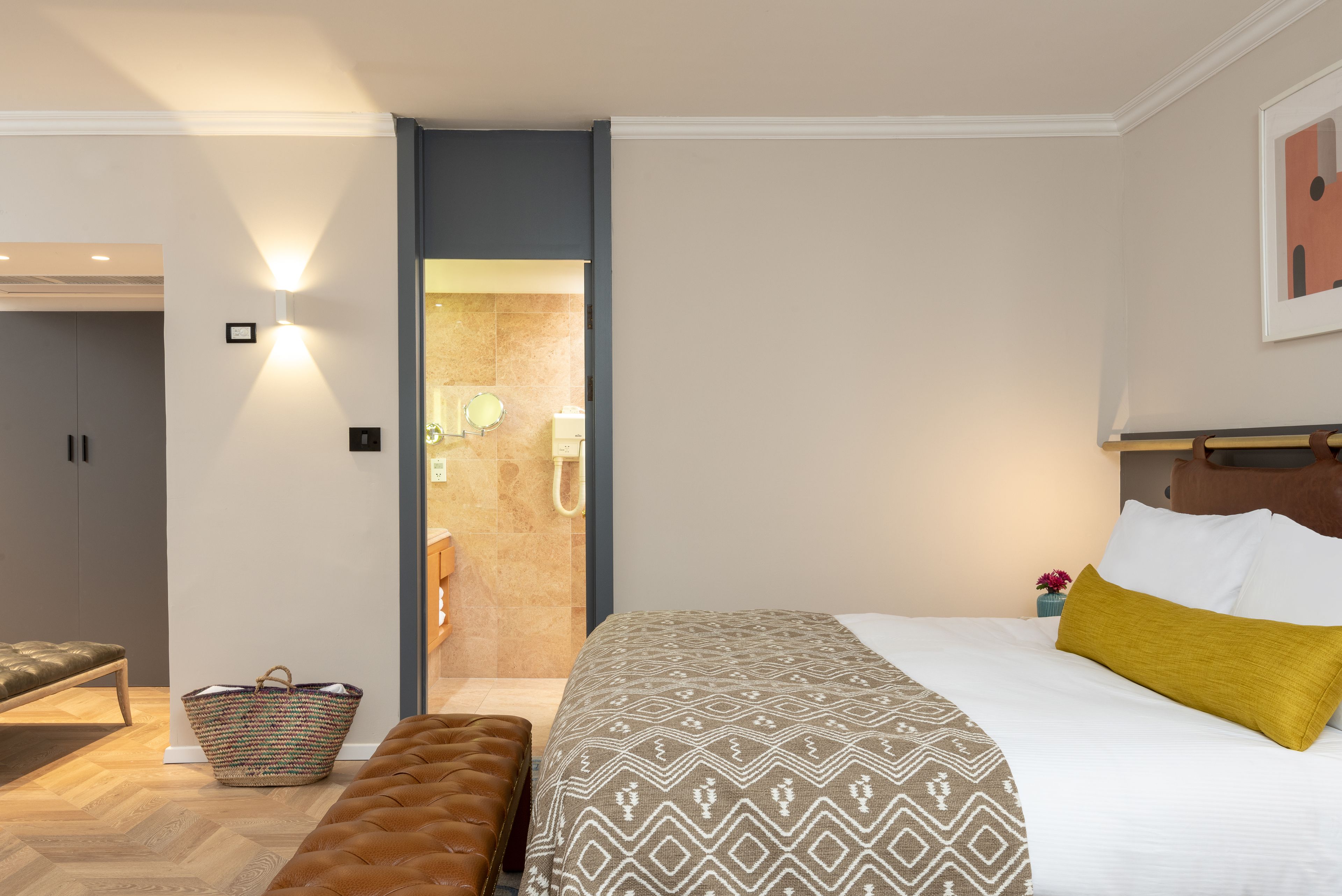 Quarto de hotel com cama, um banco, um cesto e área de chuveiro.