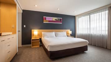 Quarto de hotel com cama grande, mesas de cabeceira, guarda-roupa e vista para a cidade pela janela.