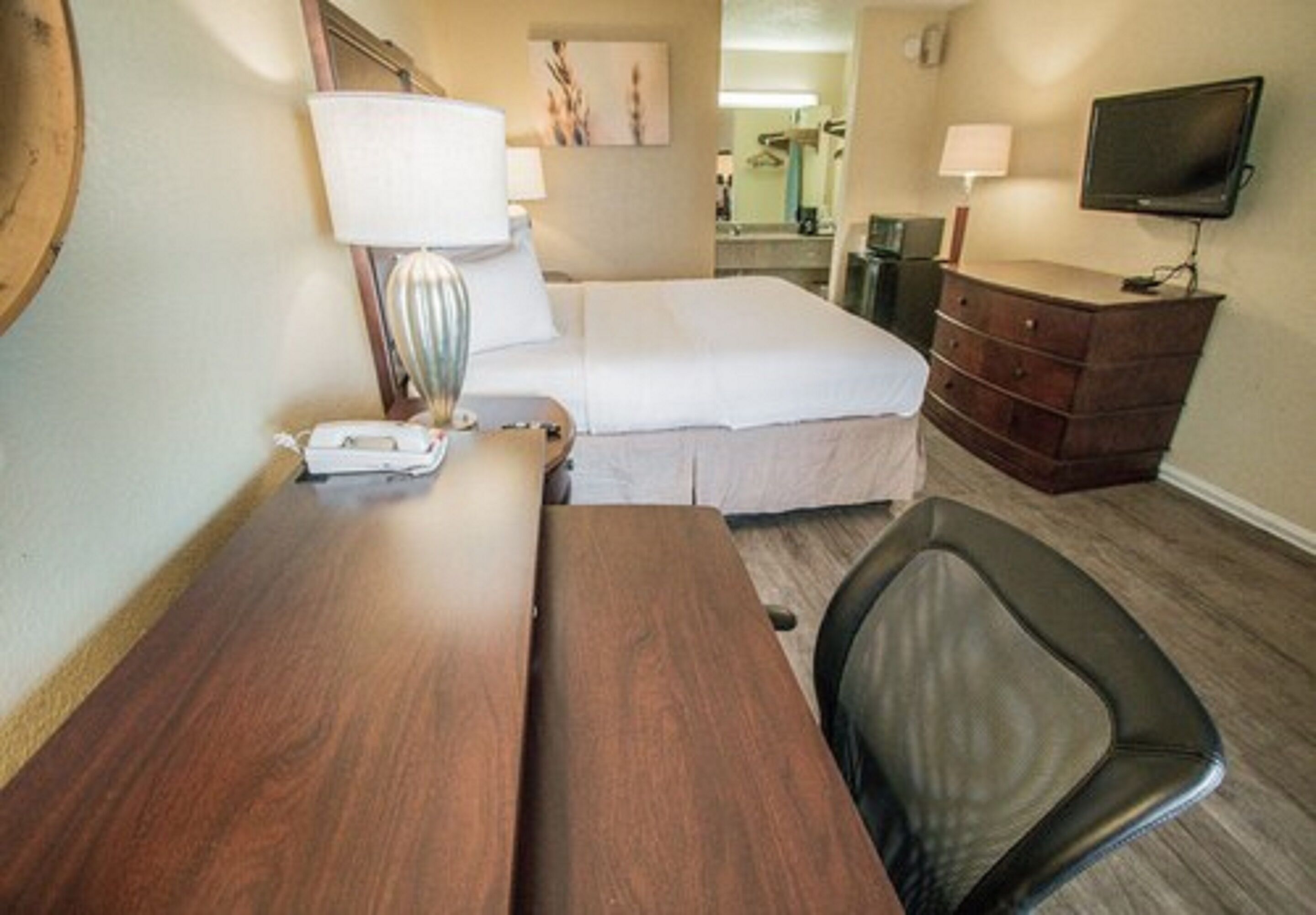 Quarto de hotel com cama, escrivaninha com telefone, cadeira, cômoda e televisão fixada na parede.
