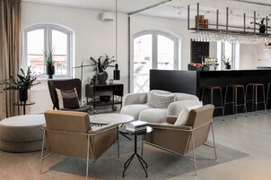 Uma sala de estar moderna com sofá, cadeiras, mesa de centro e área de cozinha com banquetas.