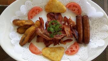 Prato de comida com bacon, linguiça e alimentos fritos sobre um prato branco com rendado.