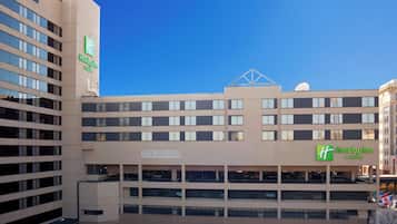 Edifício de vários andares do Holiday Inn & Suites com um logotipo 'H' em destaque, grandes janelas e uma garagem subterrânea.