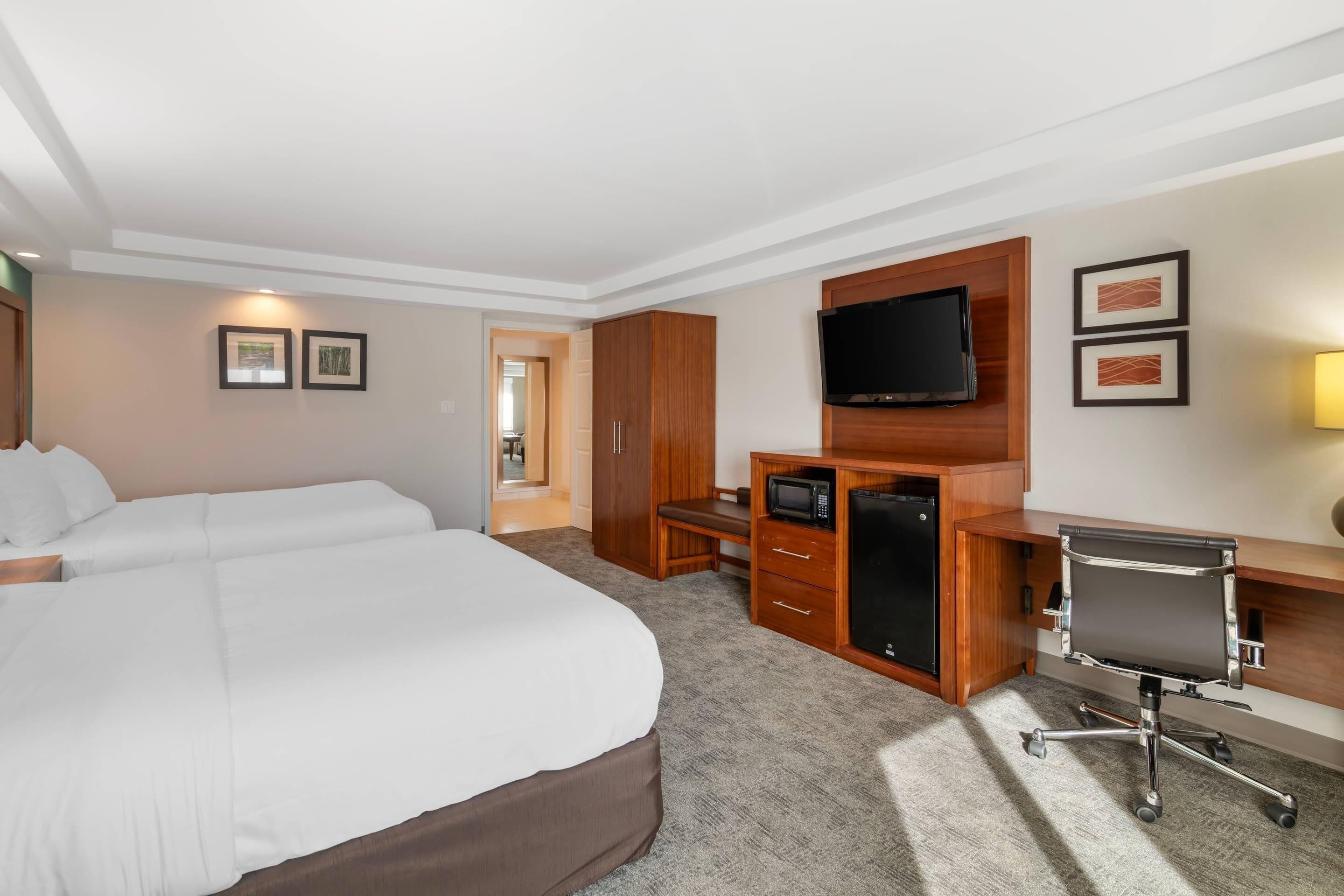 Quarto de hotel com uma cama grande, uma escrivaninha com computador, televisão e micro-ondas.