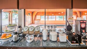 Disposição de buffet de café da manhã com diversos alimentos e dispensadores de bebidas.
