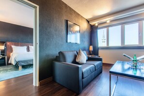 Quarto de hotel moderno com um sofá de couro escuro, uma mesa de centro de vidro e uma grande janela com vista para uma torre.
