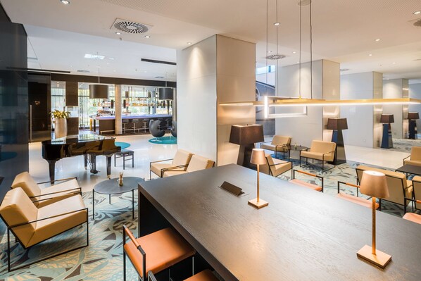 Um lobby de hotel moderno com um balcão de recepção alongado, áreas de estar confortáveis e um bar/lounge com piano.
