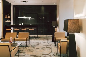 Um hall de hotel moderno com área de bar, sofás e um tapete estampado.