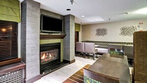 Uma sala de estar moderna com lareira, uma TV de tela plana acima dela e uma área de jantar com assento estofado e cadeiras.
