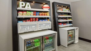 Exposição de petiscos com diversos alimentos embalados e uma área refrigerada com água engarrafada.
