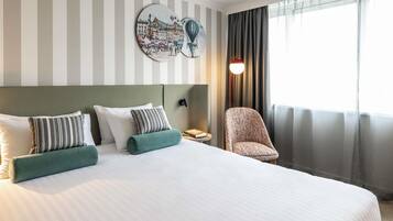 Quarto de hotel com uma cama grande, decoração de parede listrada, uma cadeira e uma janela com cortinas.