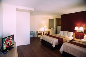Quarto de hotel com duas camas, televisão, escrivaninha com cadeira e luminária.