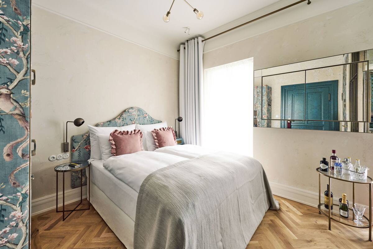 Quarto com cama, mesa de cabeceira, espelho e pequena mesa com garrafas.