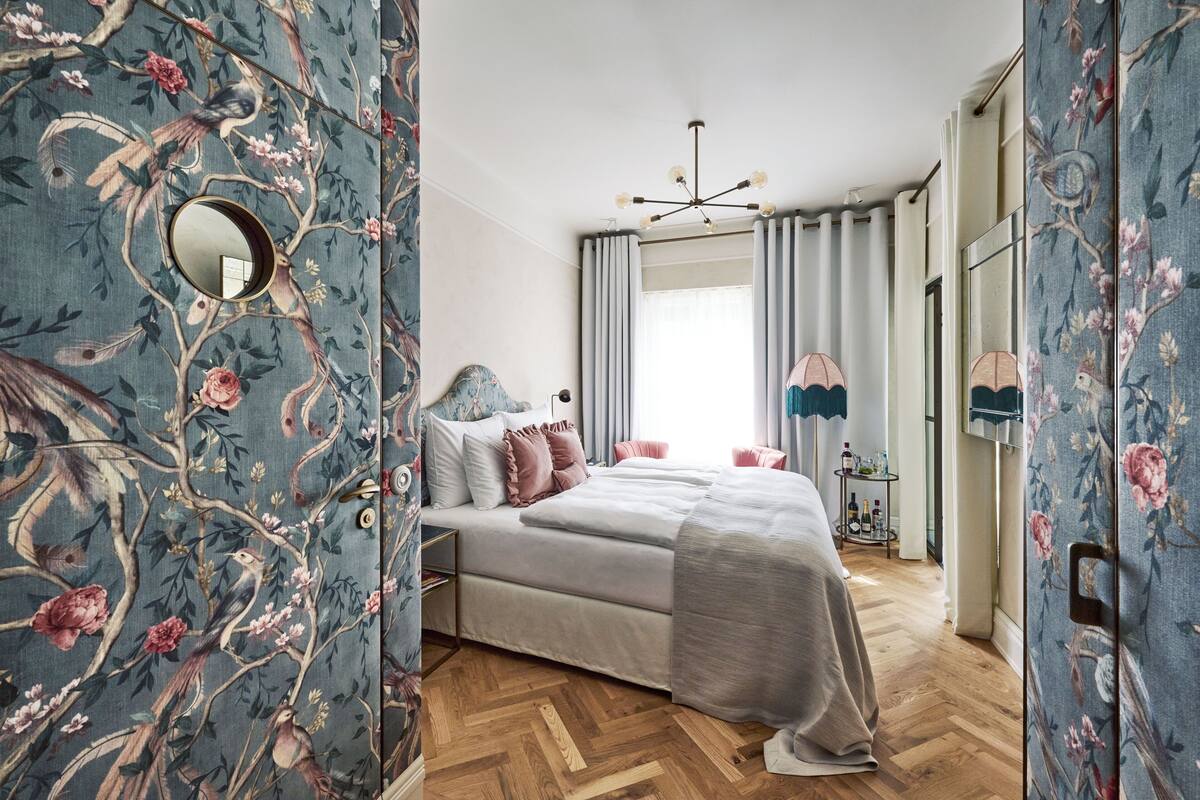 Quarto com cama, espelho, lustre e papel de parede floral.