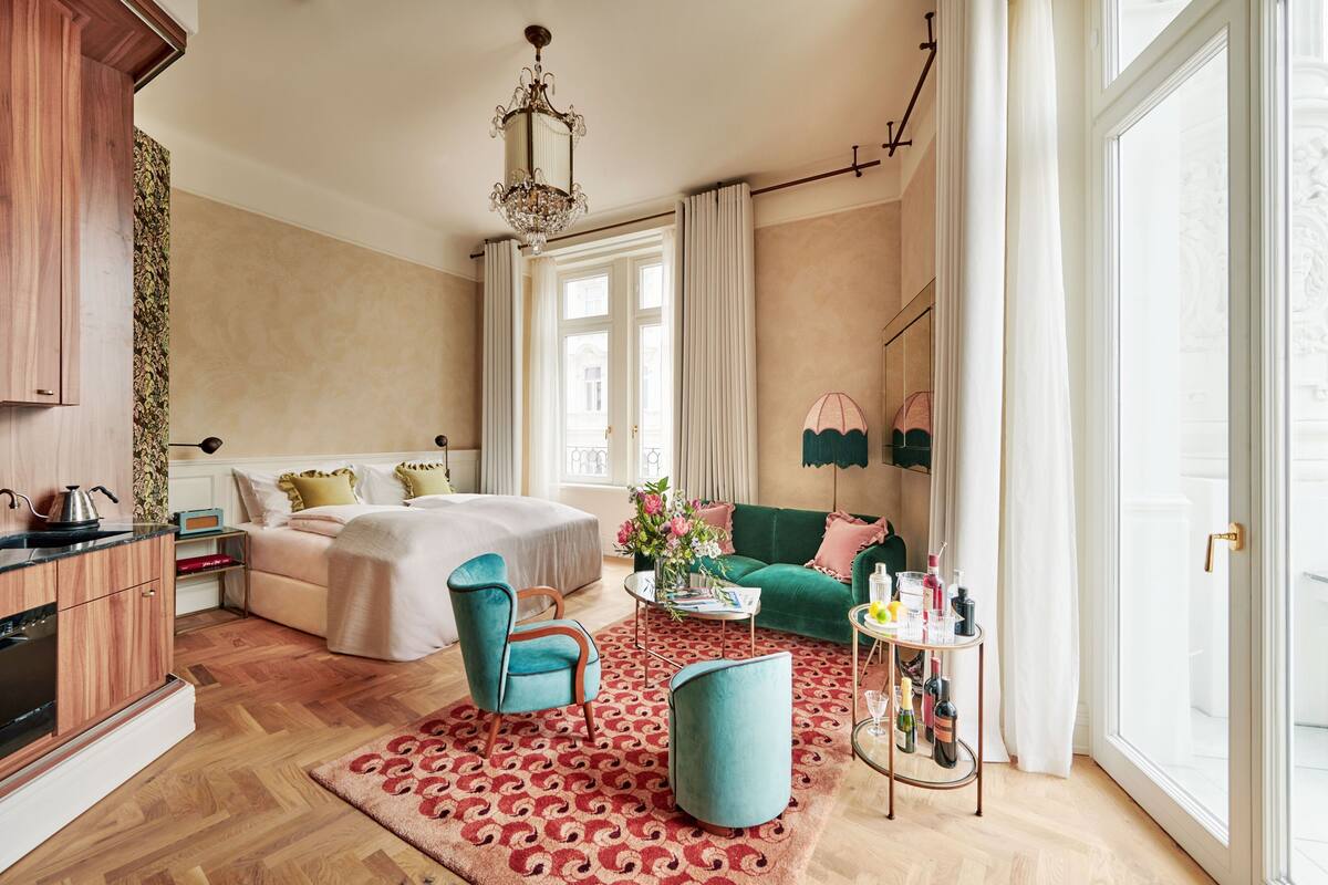 Um quarto espaçoso com uma cama grande, um sofá verde, um tapete vermelho estampado e um candelabro.