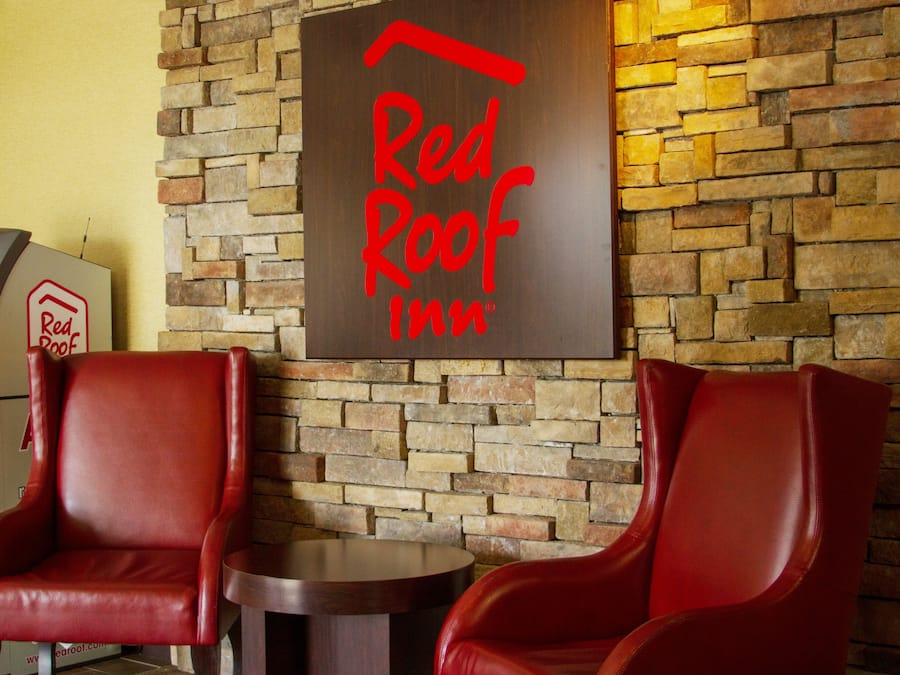 Placa da Red Roof Inn em uma parede de tijolos, com duas poltronas de couro e uma mesa pequena.