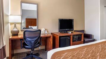 Quarto de hotel com cama, escrivaninha com computador, televisão, micro-ondas e uma cadeira.