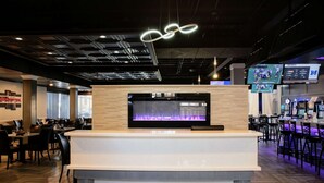Restaurante moderno com área de bar central, uma tela de televisão exibindo conteúdo esportivo e um lustre de teto marcante.