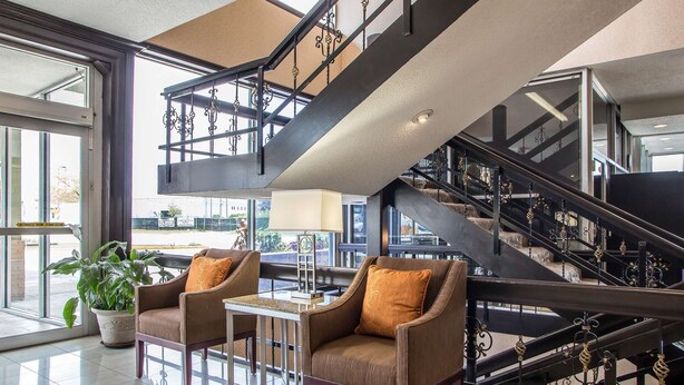 Um hall com escadas, duas poltronas, uma mesa e um vaso com planta.