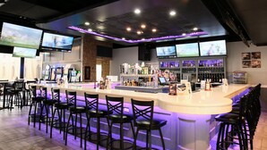 Uma área de bar com várias telas, um balcão e alguns banquetas pretas.