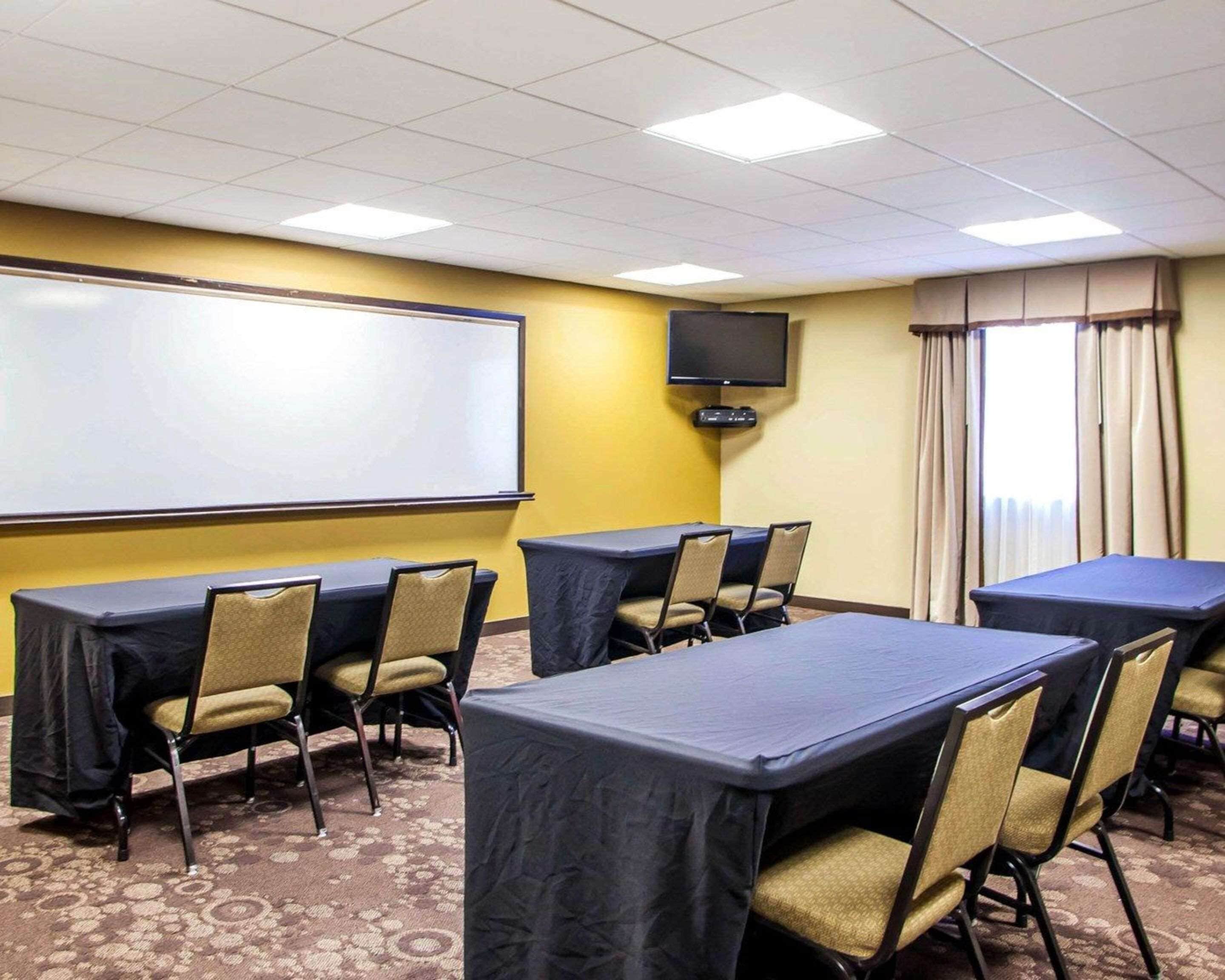 Uma sala de conferências com quadro branco, televisão de tela plana e mesas com cadeiras.