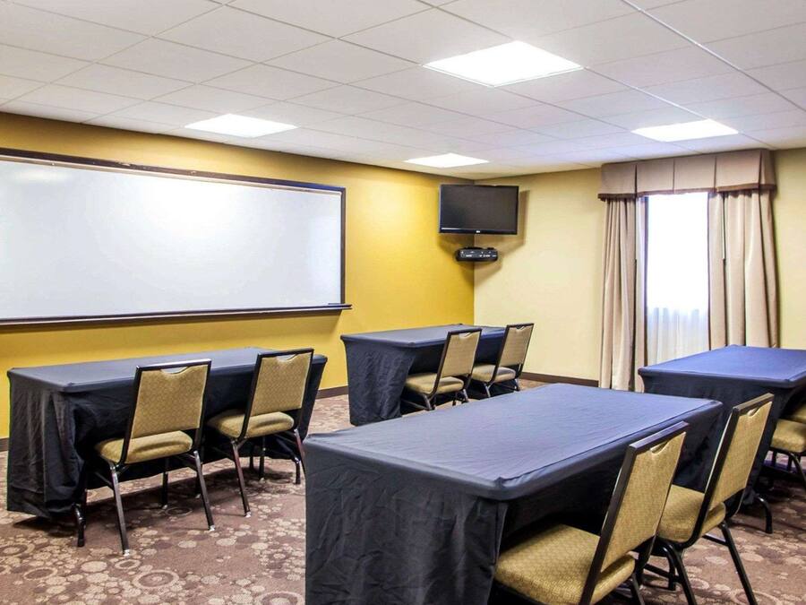 Uma sala de conferências com quadro branco, televisão de tela plana e mesas com cadeiras.