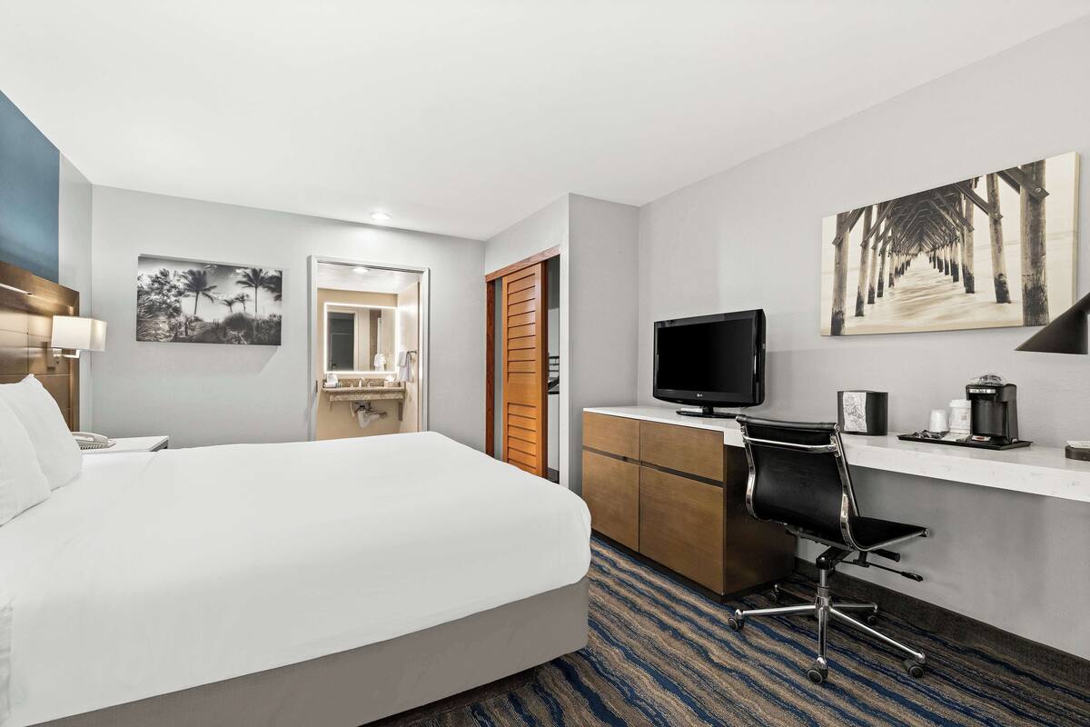 Quarto de hotel com uma cama grande, uma mesa com cadeira, televisão e obras de arte nas paredes.