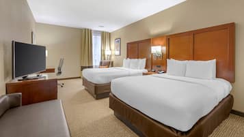 Quarto de hotel com duas camas, uma mesa com televisão de tela plana, uma cadeira, um abajur e uma janela com cortinas.