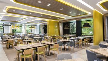 Um restaurante espaçoso com várias áreas de refeições, iluminação moderna e grandes janelas com vista para o verde.