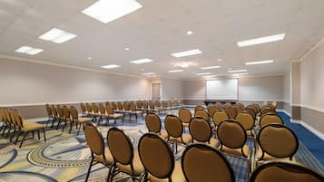 Uma sala de conferências com fileiras de cadeiras, palco e piso coberto de carpete.